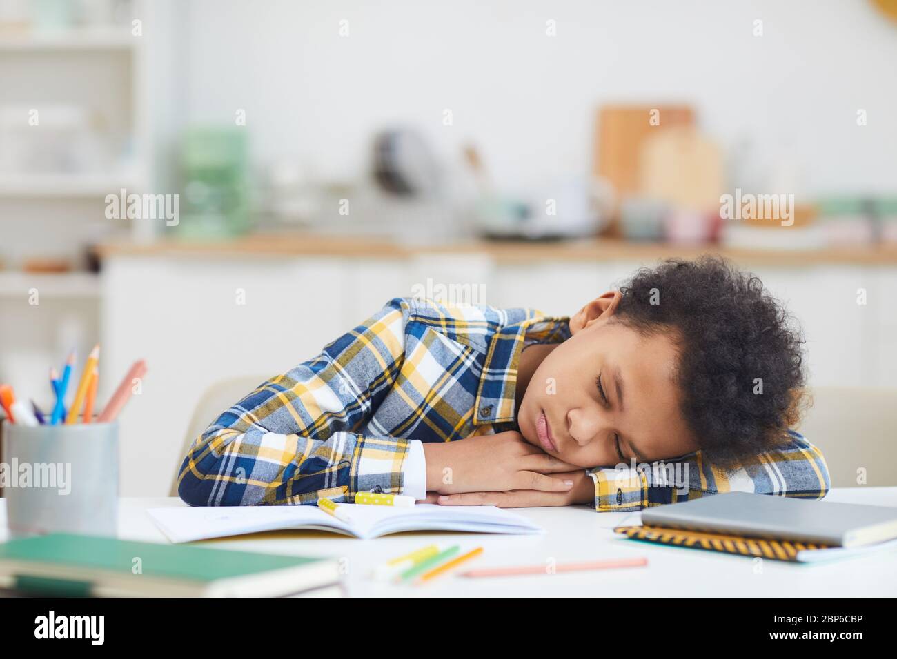 Portrait of exhausted African-American boy sleeping at desk while doing ...
