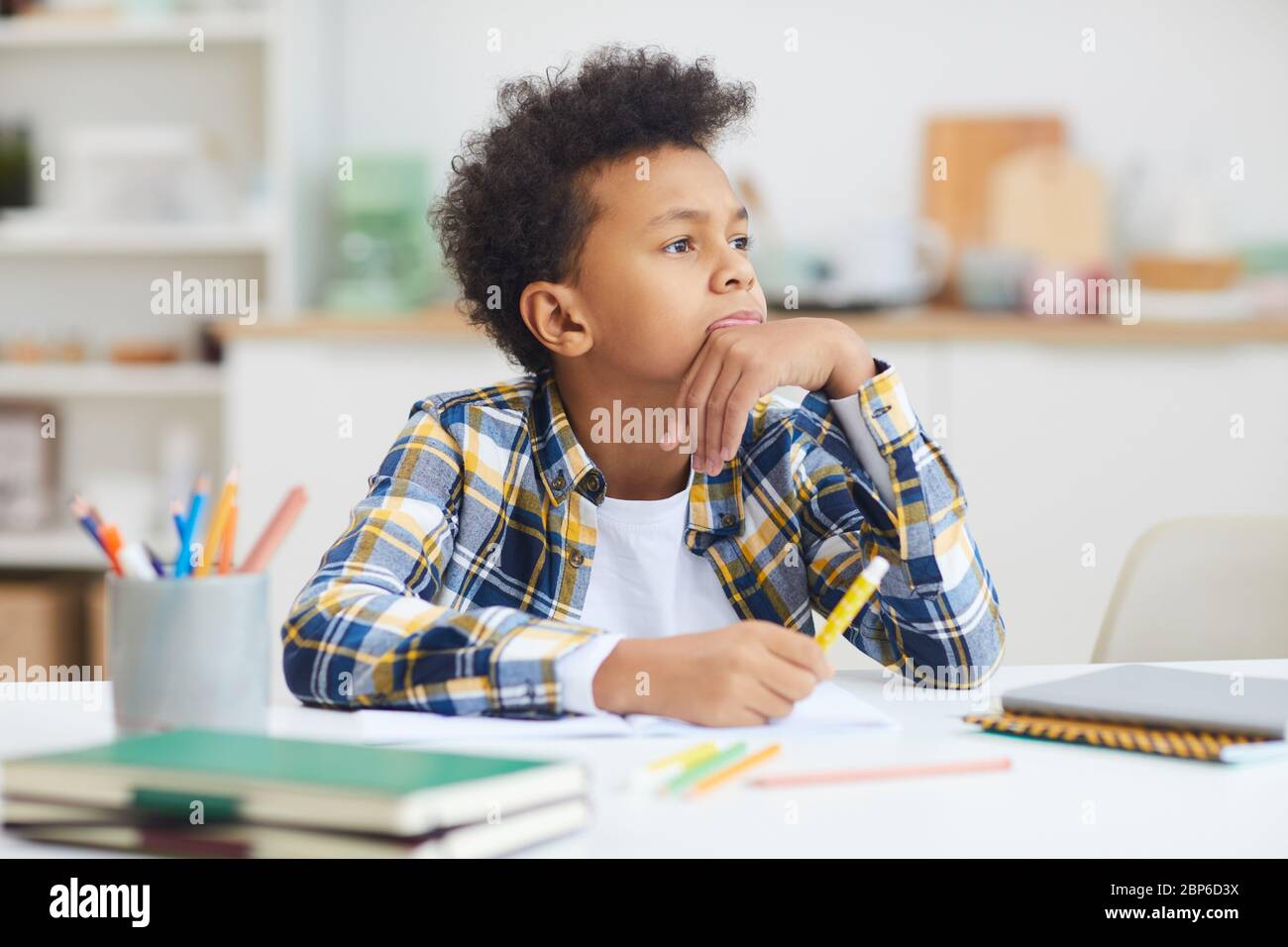 Portrait of teenage African-American boy daydreaming at desk while ...