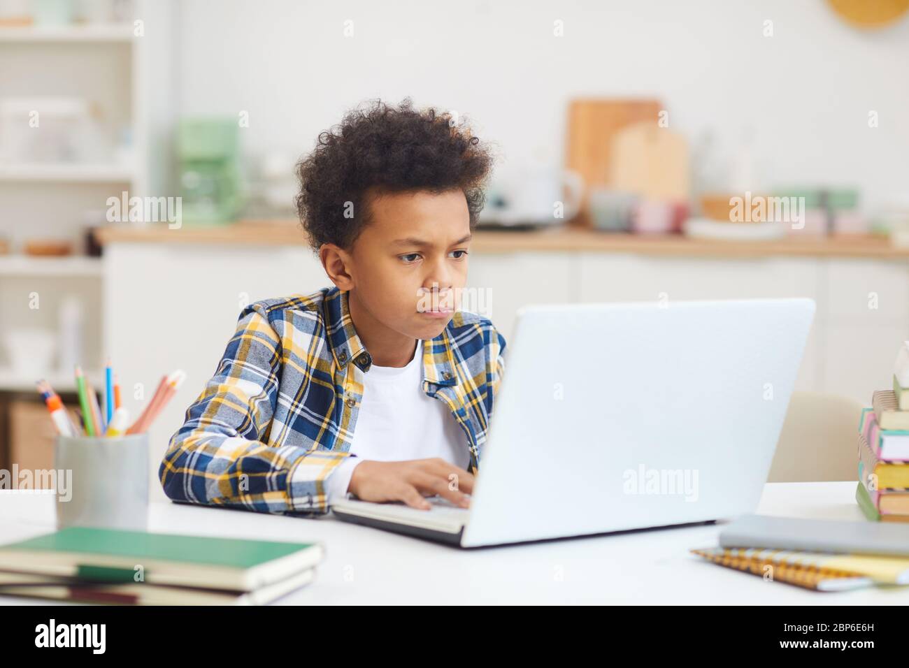 Portrait of teenage African boy using laptop while studying at home ...