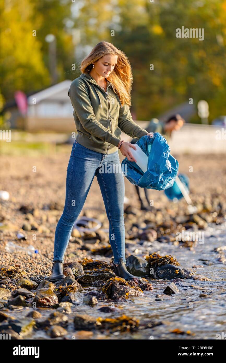 Young woman picking up garbage from rocky shore Stock Photo - Alamy