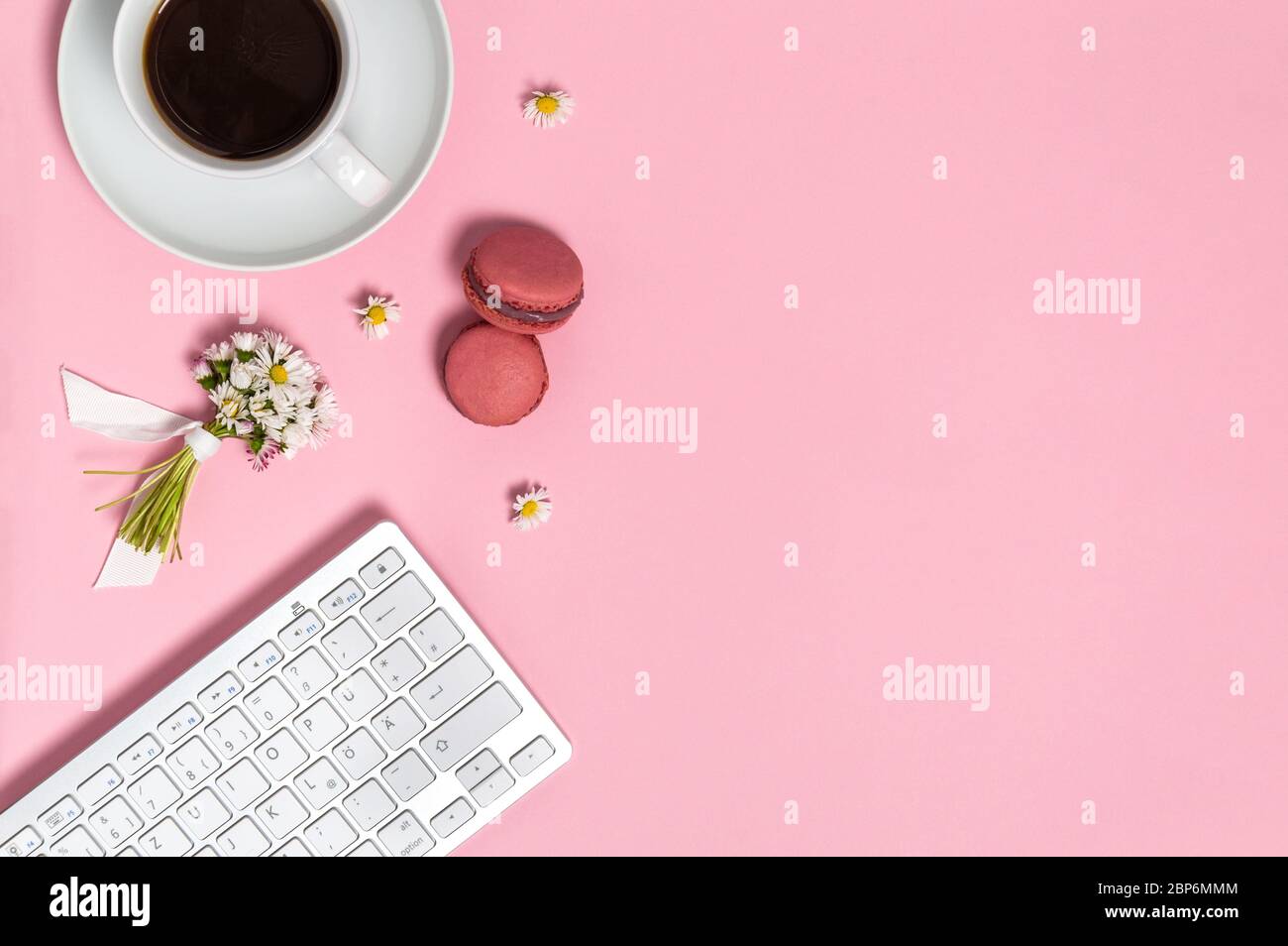 Female workspace with keyboard, cup of black coffee, two macarons and ...