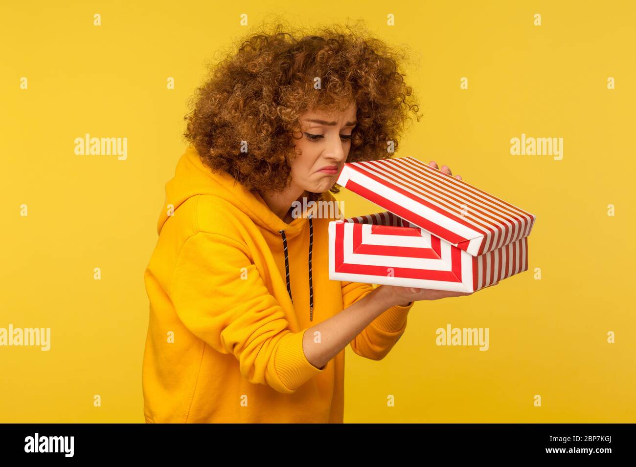 Portrait of upset displeased curly-haired woman in hoodie looking into ...