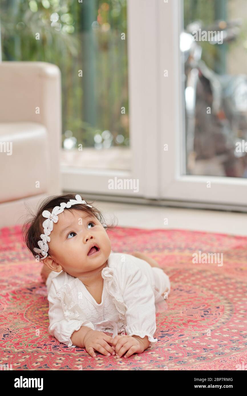 Curious little baby girl crawling on the floor at looking up at ...