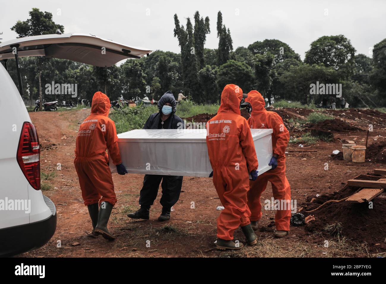 Cemetery workers carry a coffin while dressed in protective suits as a ...