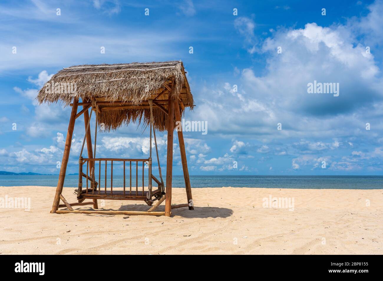 Wooden Swing Under A Thatched Roof On A Sandy Tropical Beach Near The