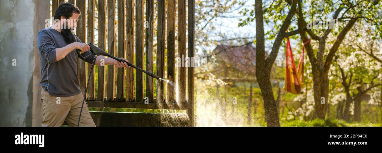Mid adult caucasian man cleaning a wooden gate with a power washer ...