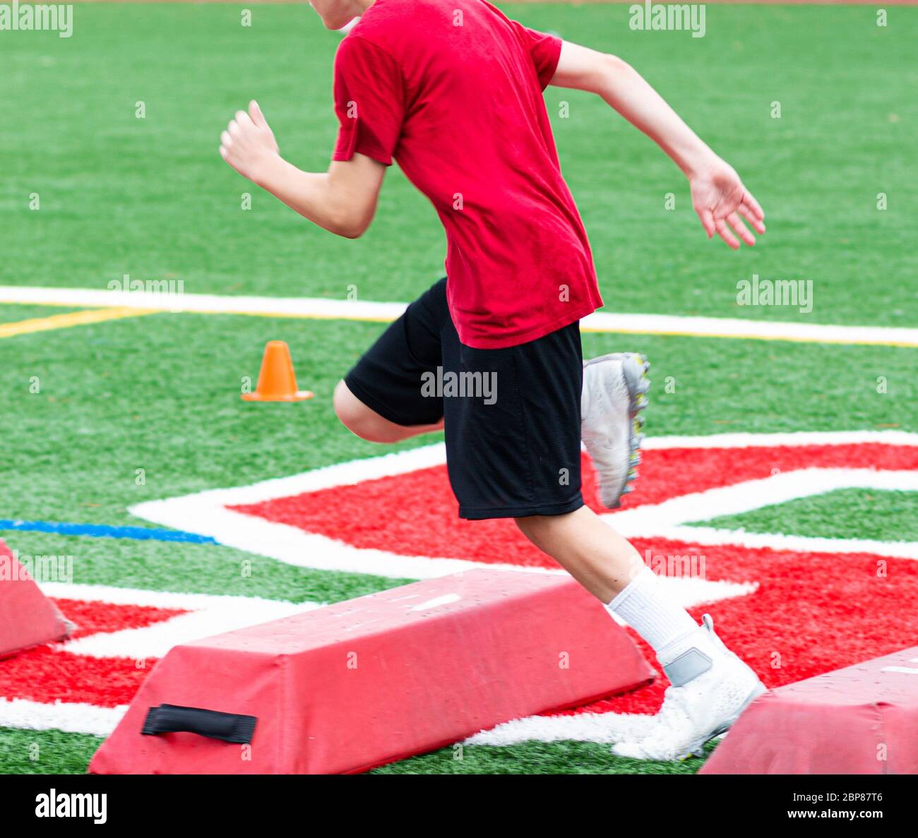 A young teenage boy is running over red barriers placed on a green turf ...