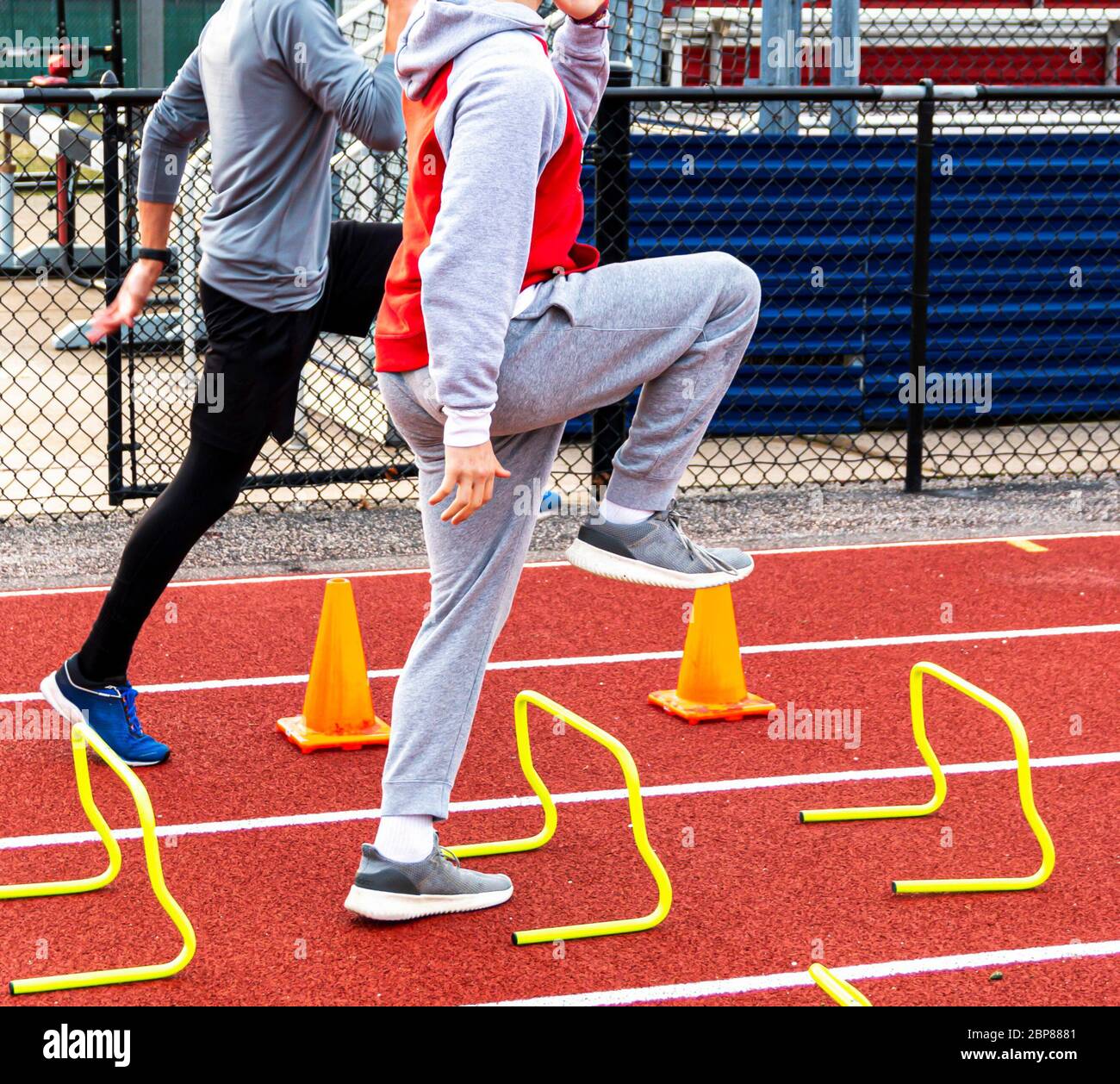 Two high school boys stepping over yellow mini hurdles and orange cones ...