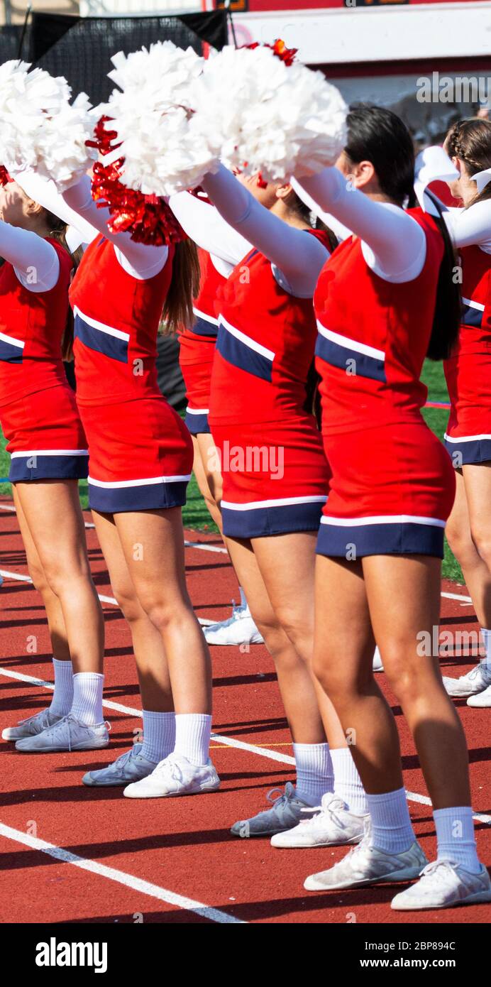 Side view of high school cheerleaders holding their pom poms up over ...