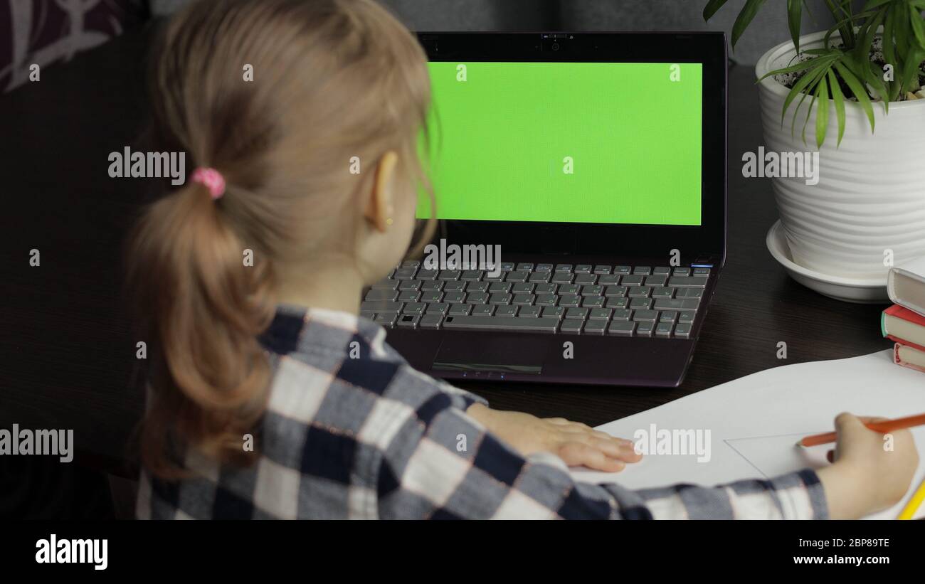 Child girl studying homework on laptop during online lesson at home. E ...