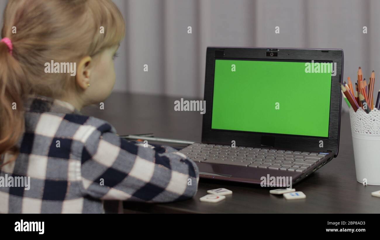 Child girl studying homework on laptop during online lesson at home. E ...