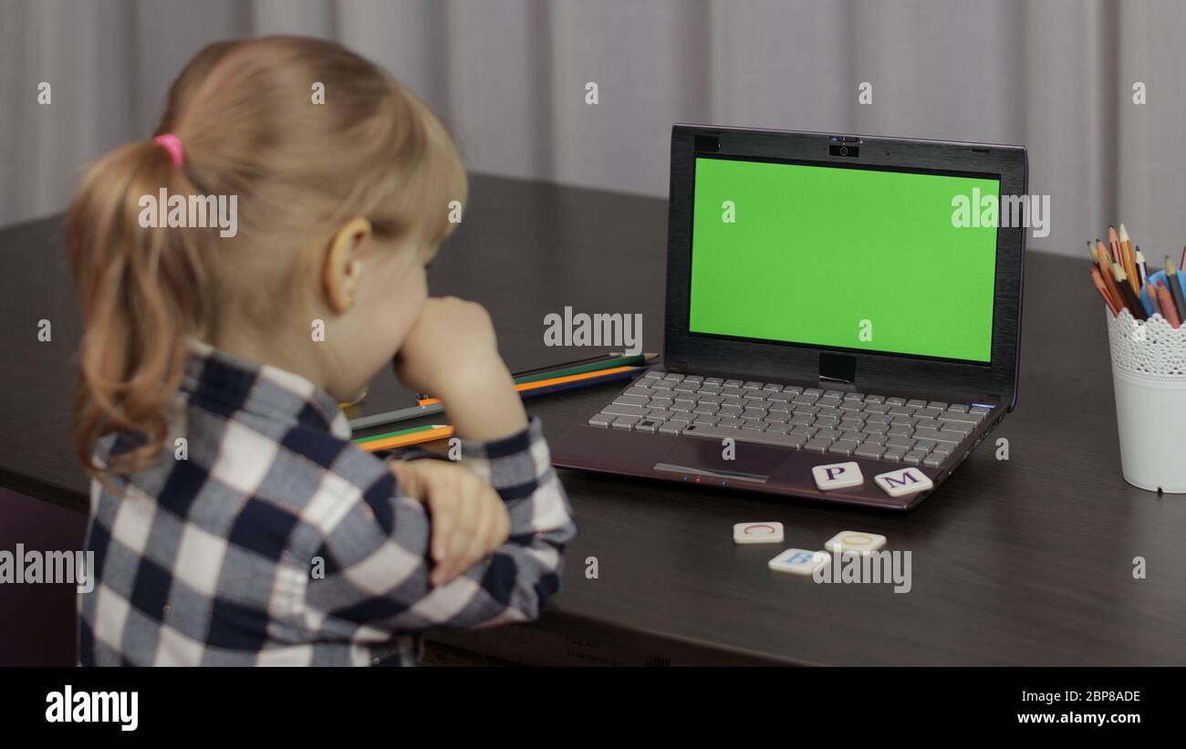 Child girl studying homework on laptop during online lesson at home. E ...