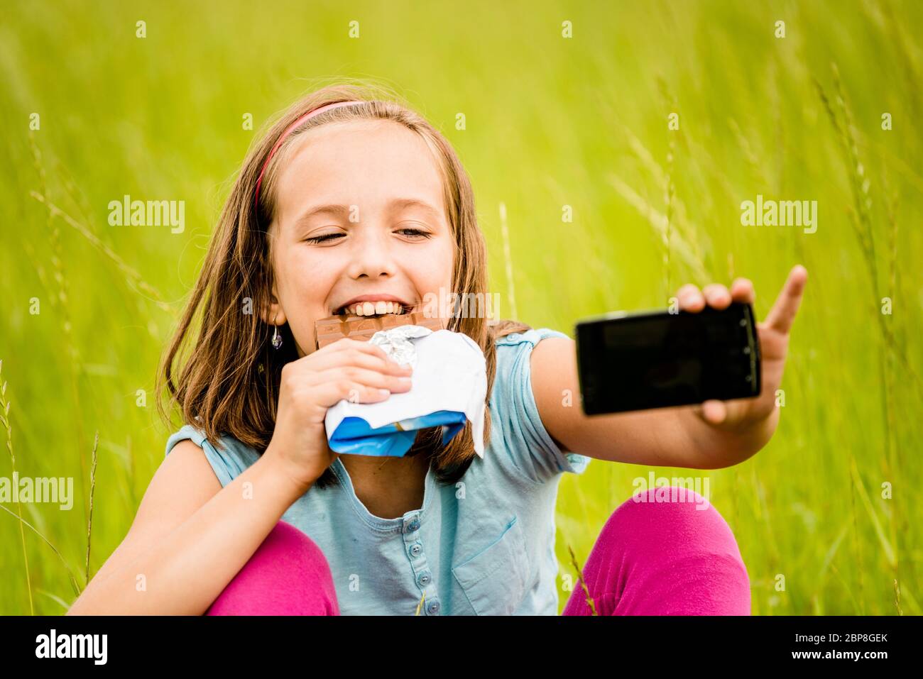 Child is taking photo with mobile phone camera while eating chocolate ...