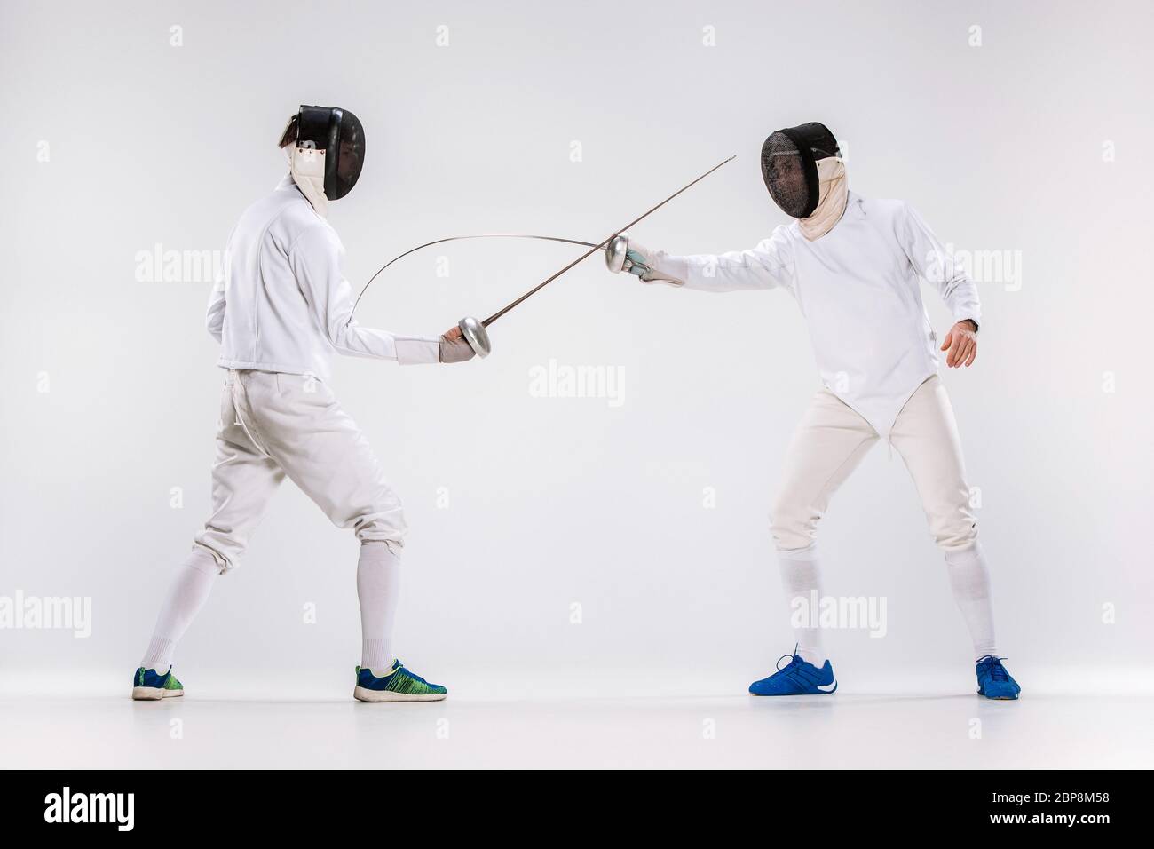 The two men wearing fencing suit practicing with sword against gray ...