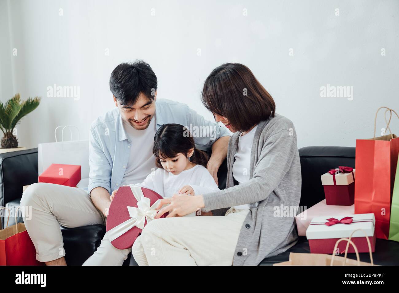 Mom and Dad and daughter at home opening presents Stock Photo - Alamy