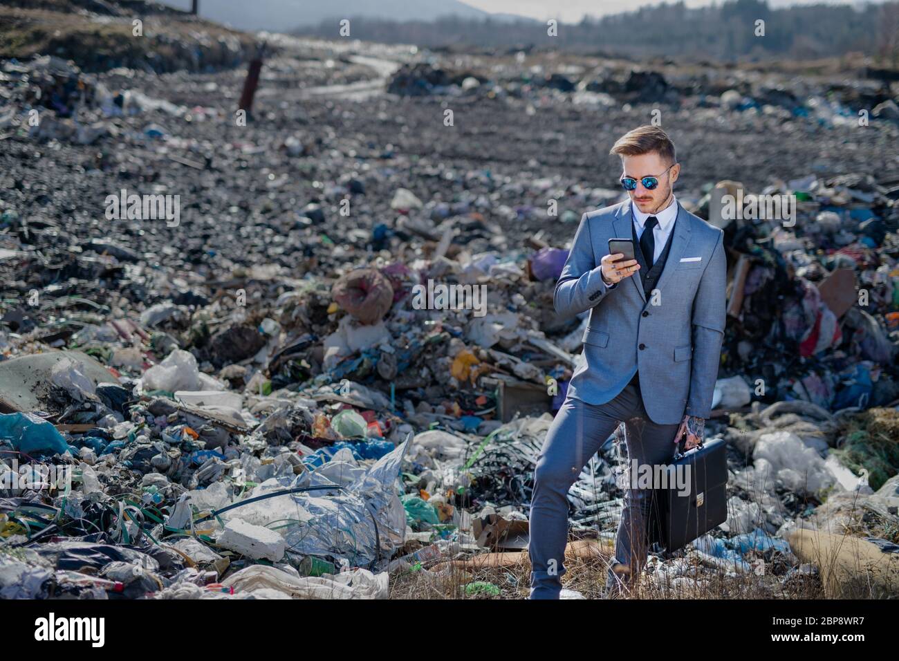 Modern businessman on landfill, consumerism versus pollution concept ...