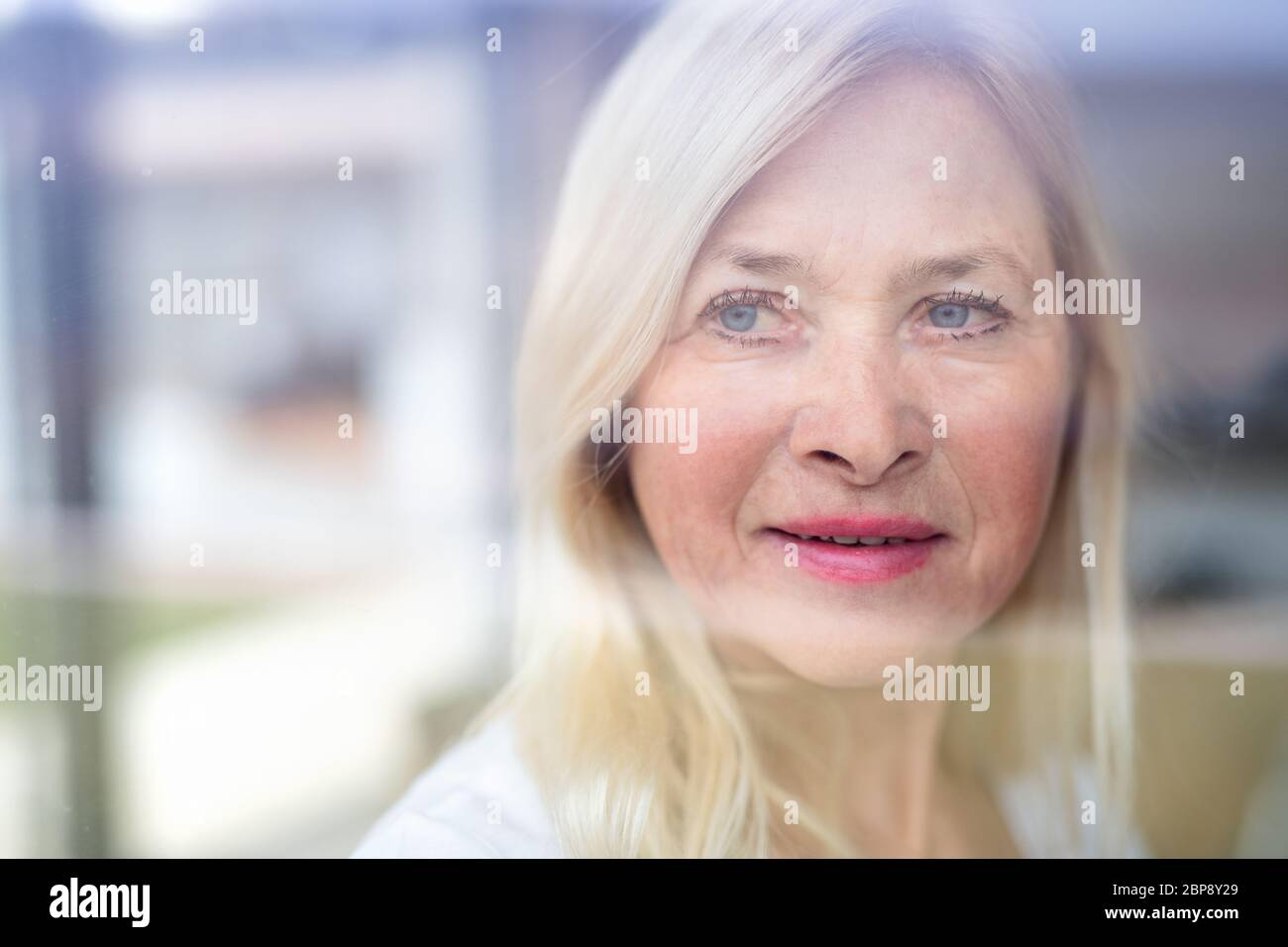 Portrait of senior woman standing indoors at home. Shot through glass ...