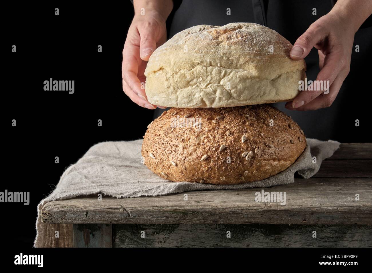 female hands holding round baked wheat flour bread over wooden table ...