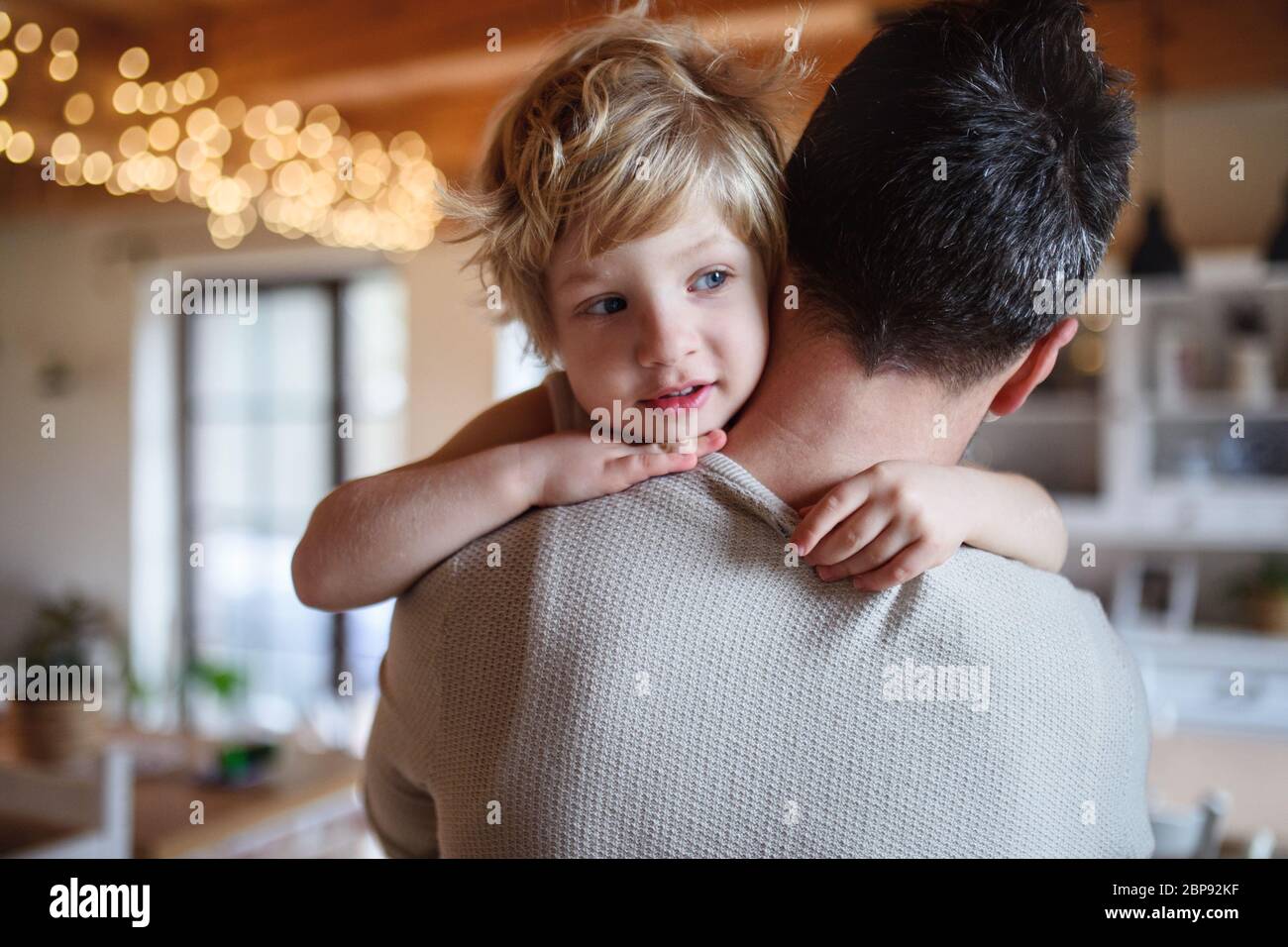 Father carrying small sick unhappy son indoors at home, comforting him ...