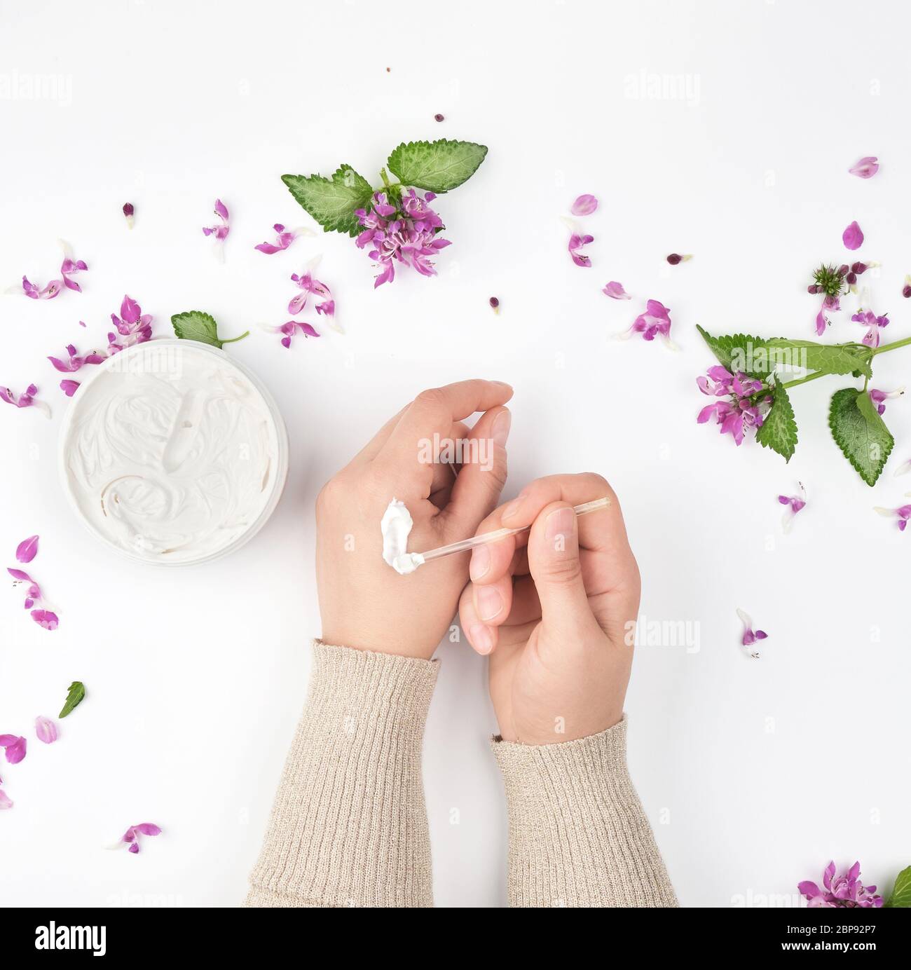 two female hands and a jar with thick cream and pink flowers with green ...