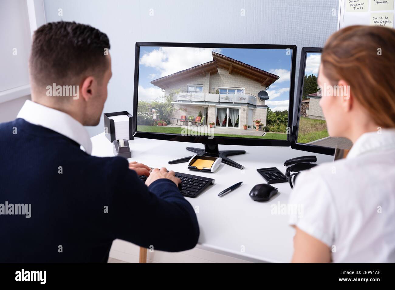 Rear View Of Male And Female Estate Agent Looking House Model On ...