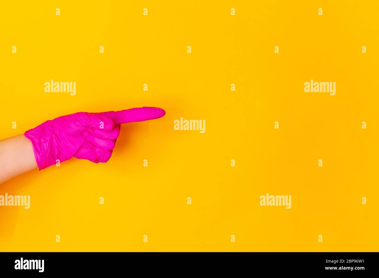 Hand in pink protective rubber glove pointing isolated on yellow studio ...