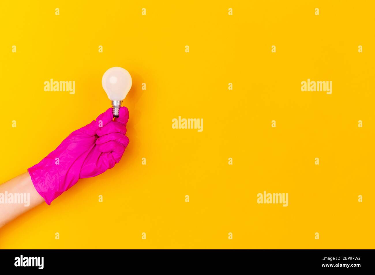 Hand in pink protective rubber glove with lightbulb isolated on yellow ...