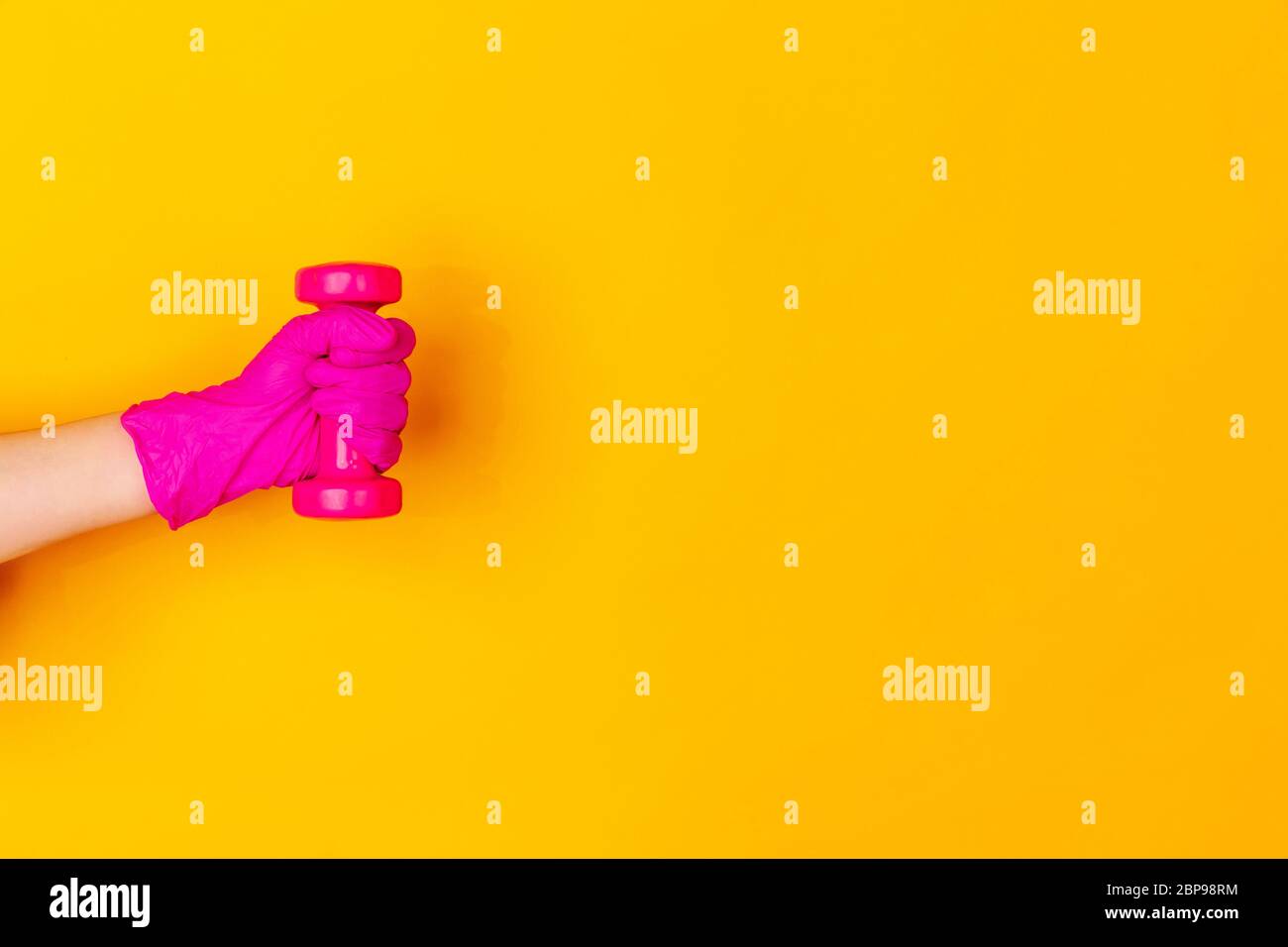 Hand in pink protective rubber glove with dumbbell isolated on yellow ...