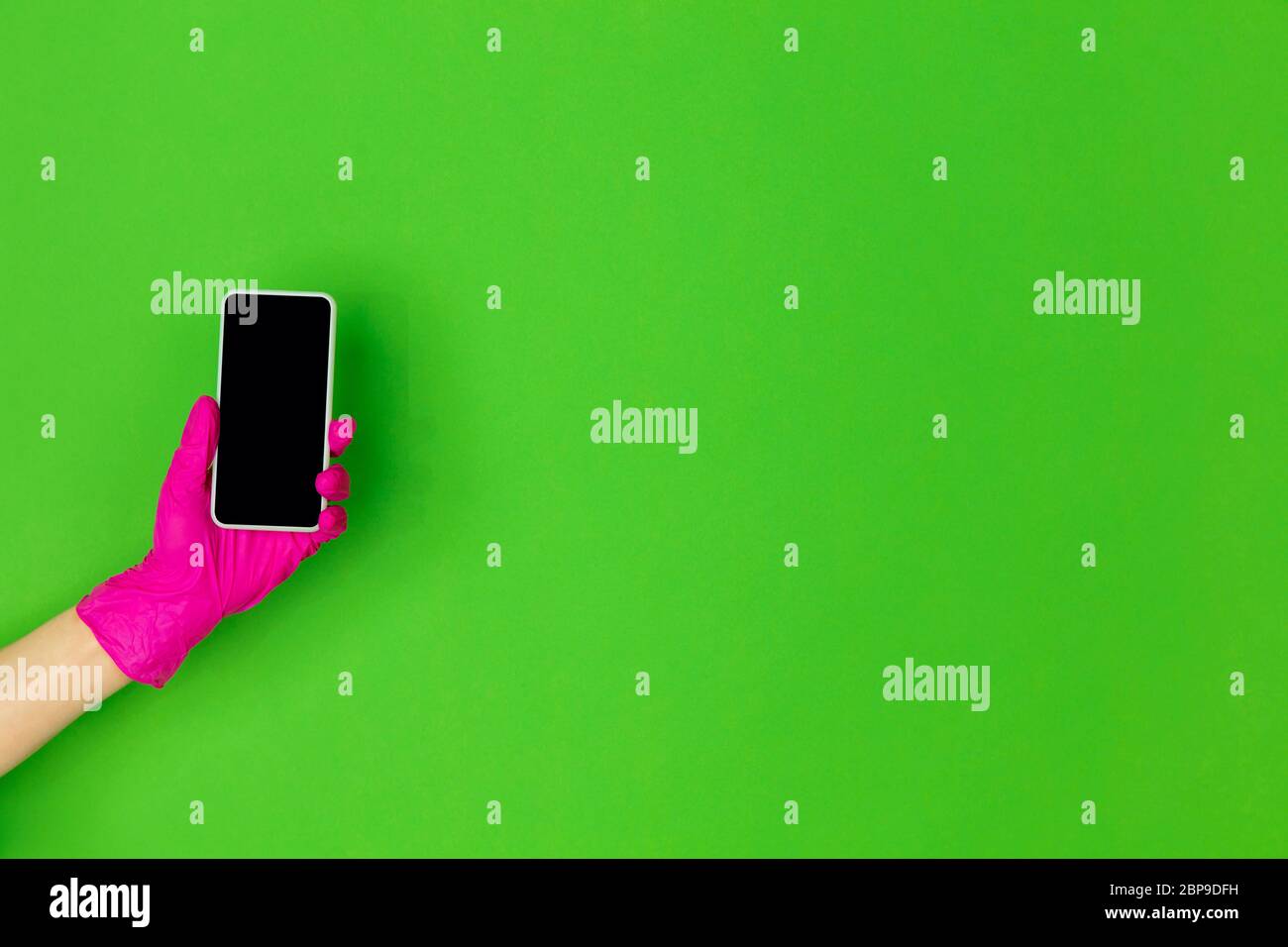 Hand in pink protective rubber glove with smartphone isolated on green ...