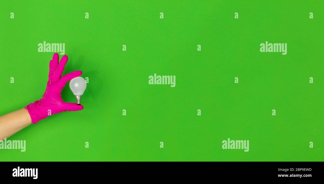 Hand in pink protective rubber glove with lightbulb isolated on green ...
