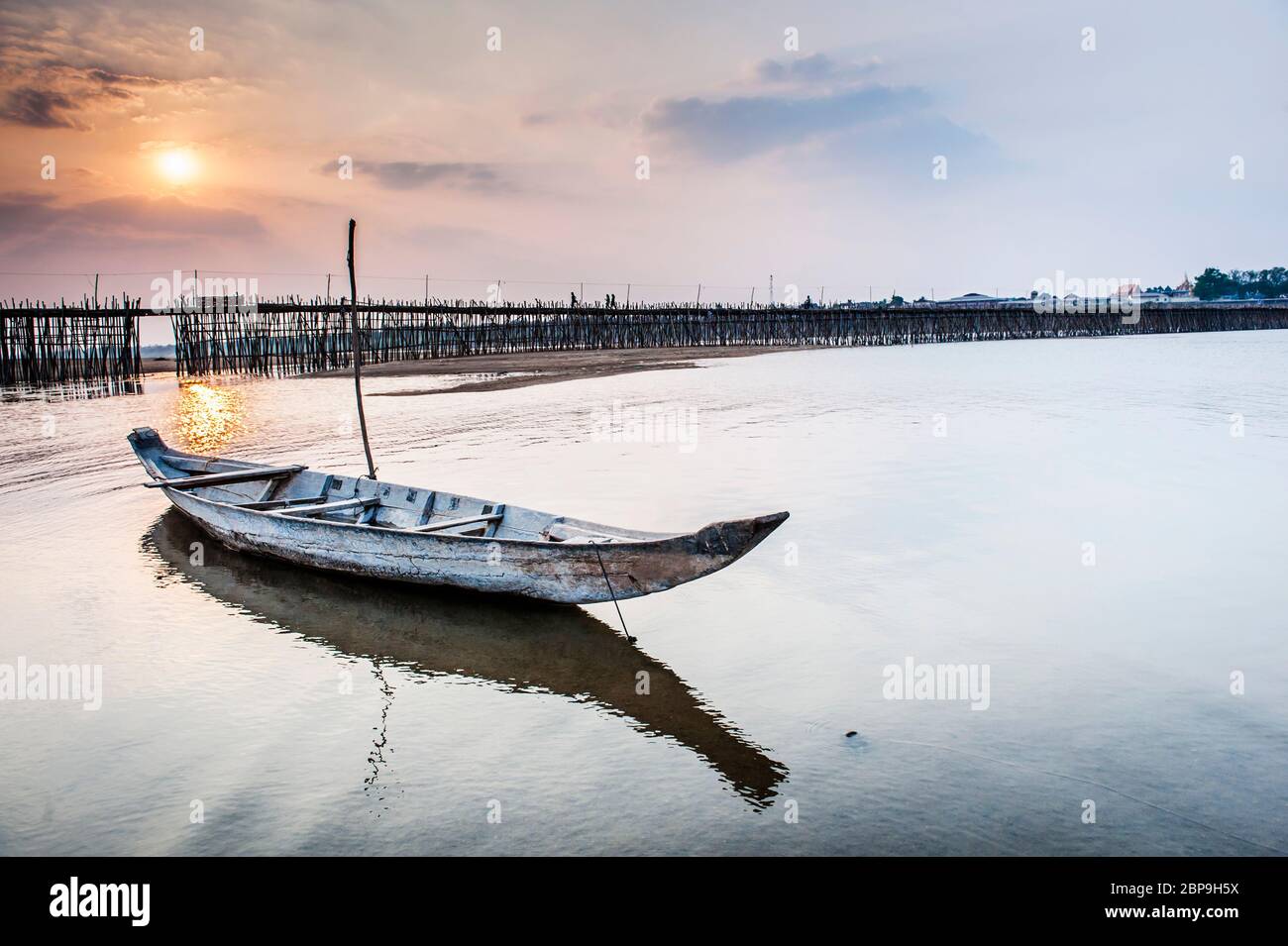 A river boat on the Mekong River at sunset with a Bamboo bridge. Ko Pen ...