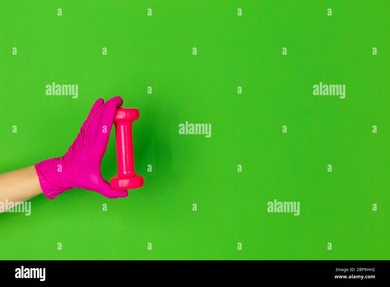 Hand in pink protective glove wth dumbbell isolated on green studio ...