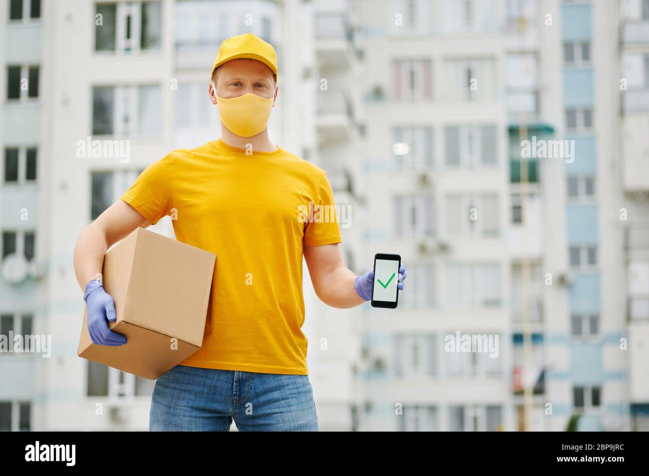 Delivery Man employee in yellow uniform cap, t-shirt, face mask and ...