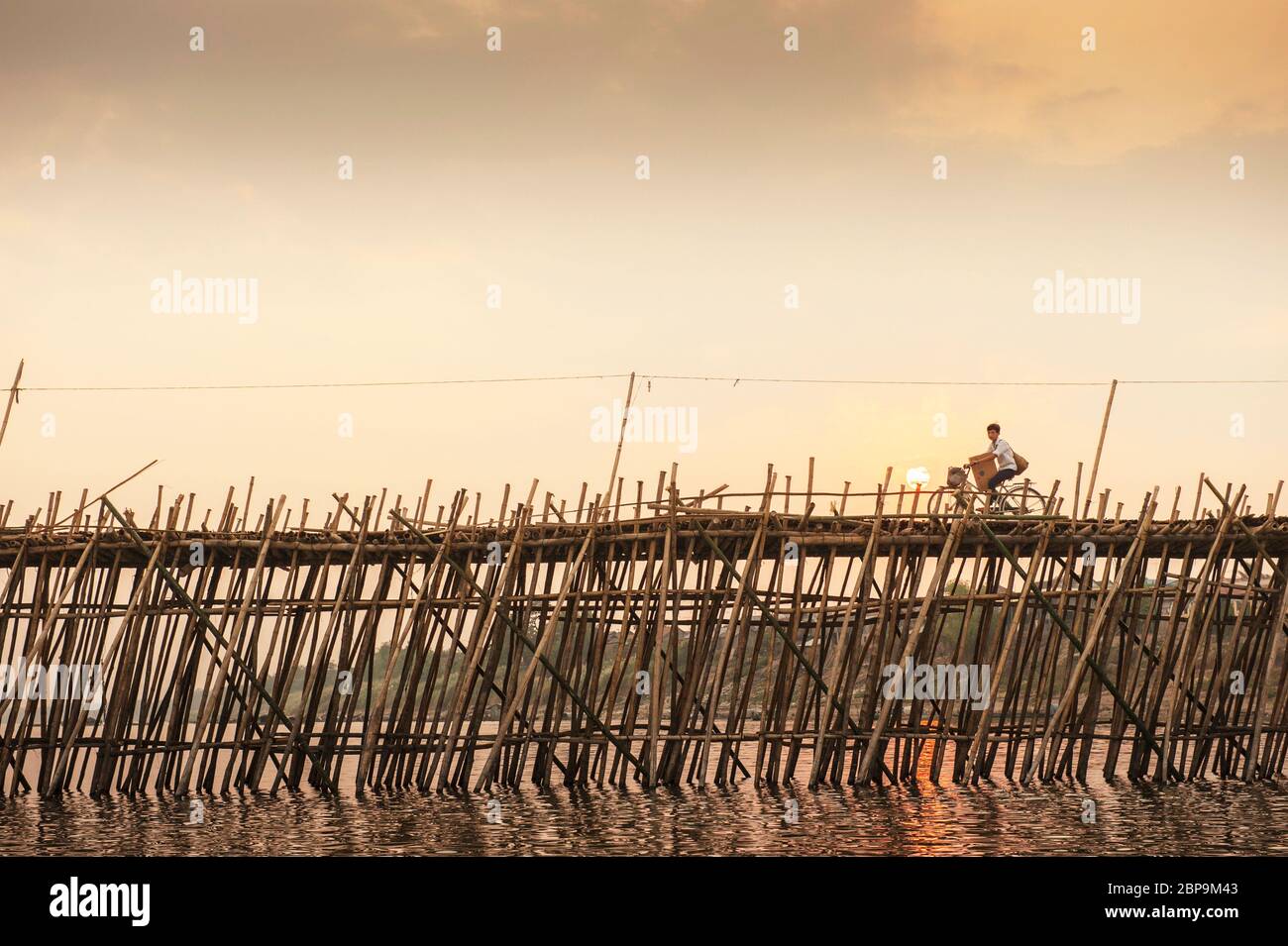A cyclist crosses a Bamboo bridge over the Mekong River at sunset. Ko ...