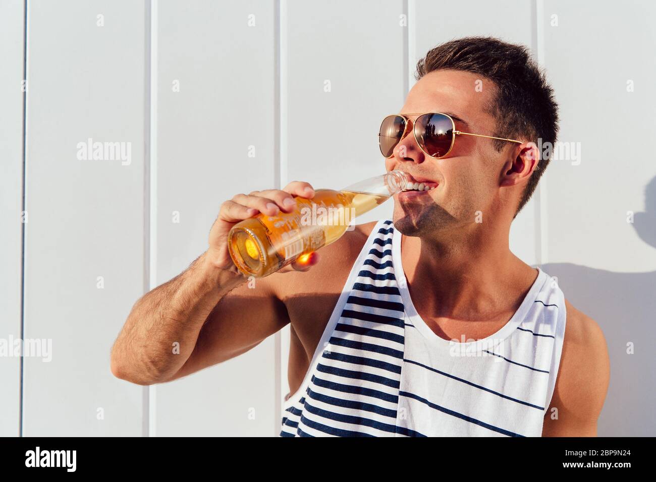 Happy young man in sunglasses drinking cold beer, standing near the ...