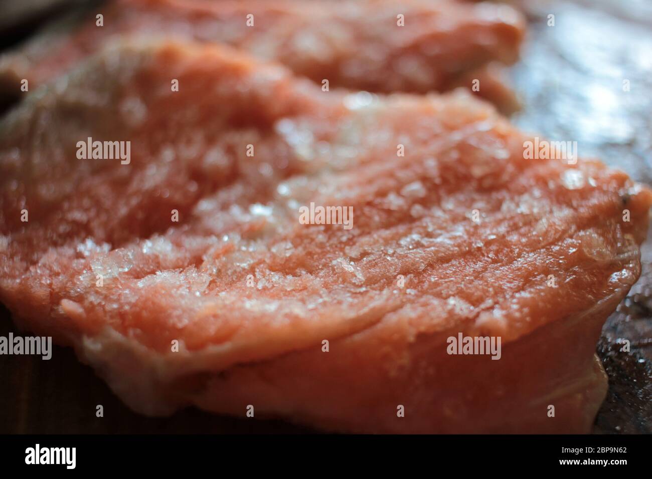 Raw salmon slices melting on a wooden cutting board. Top view of frozen ...