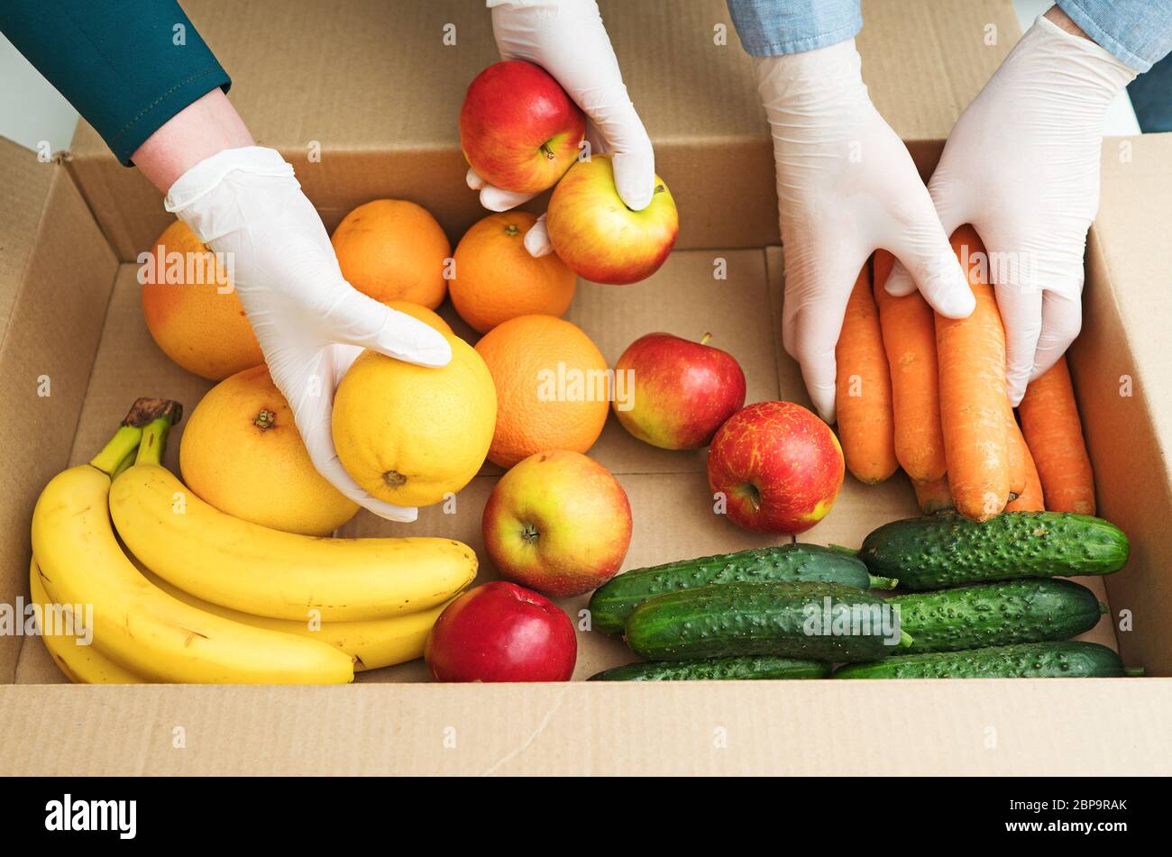 Volunteers in protective medical gloves putting fruits and vegetables ...