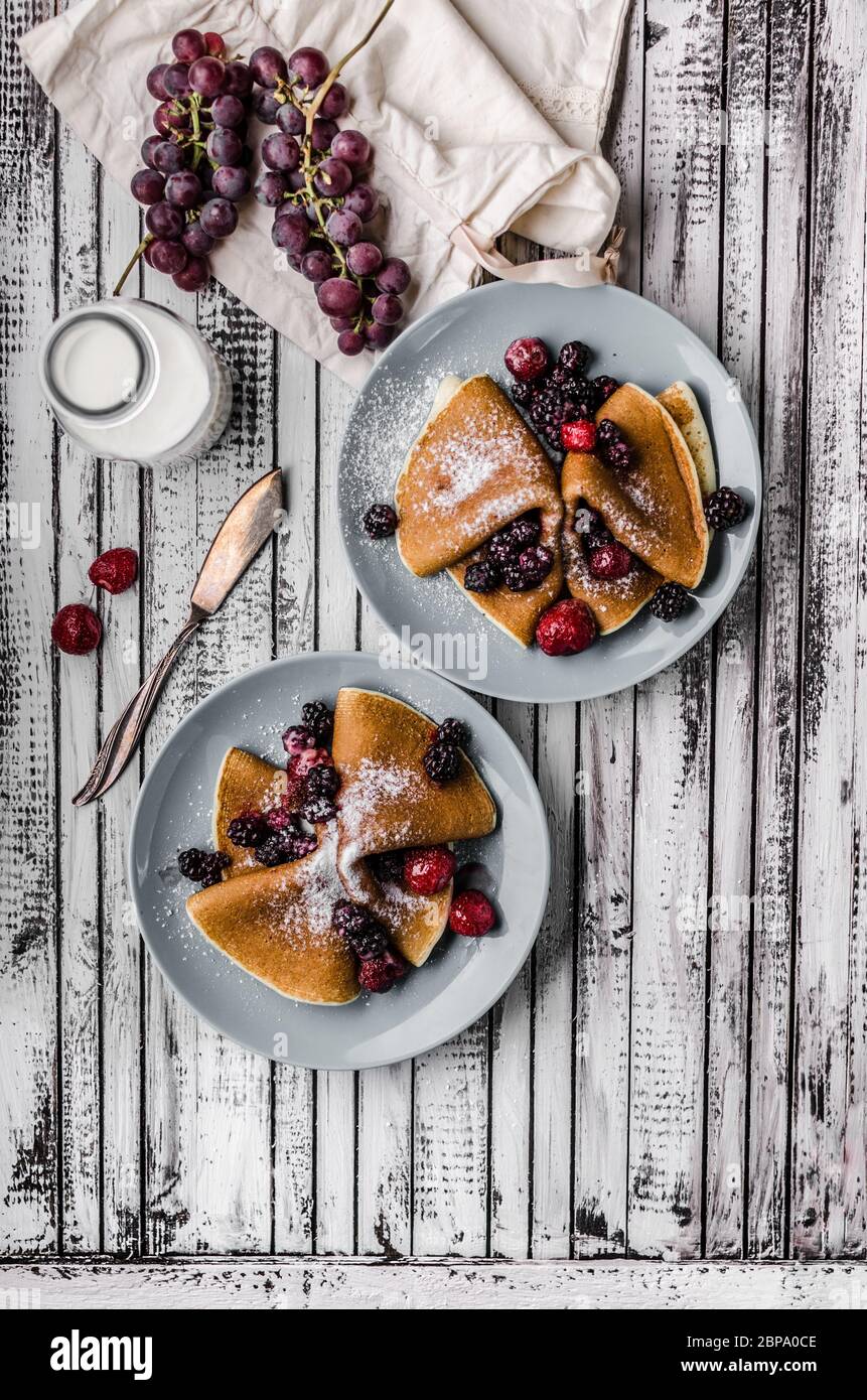 Homemade crepes with frozen berries, topped sugar, rustic wood board ...