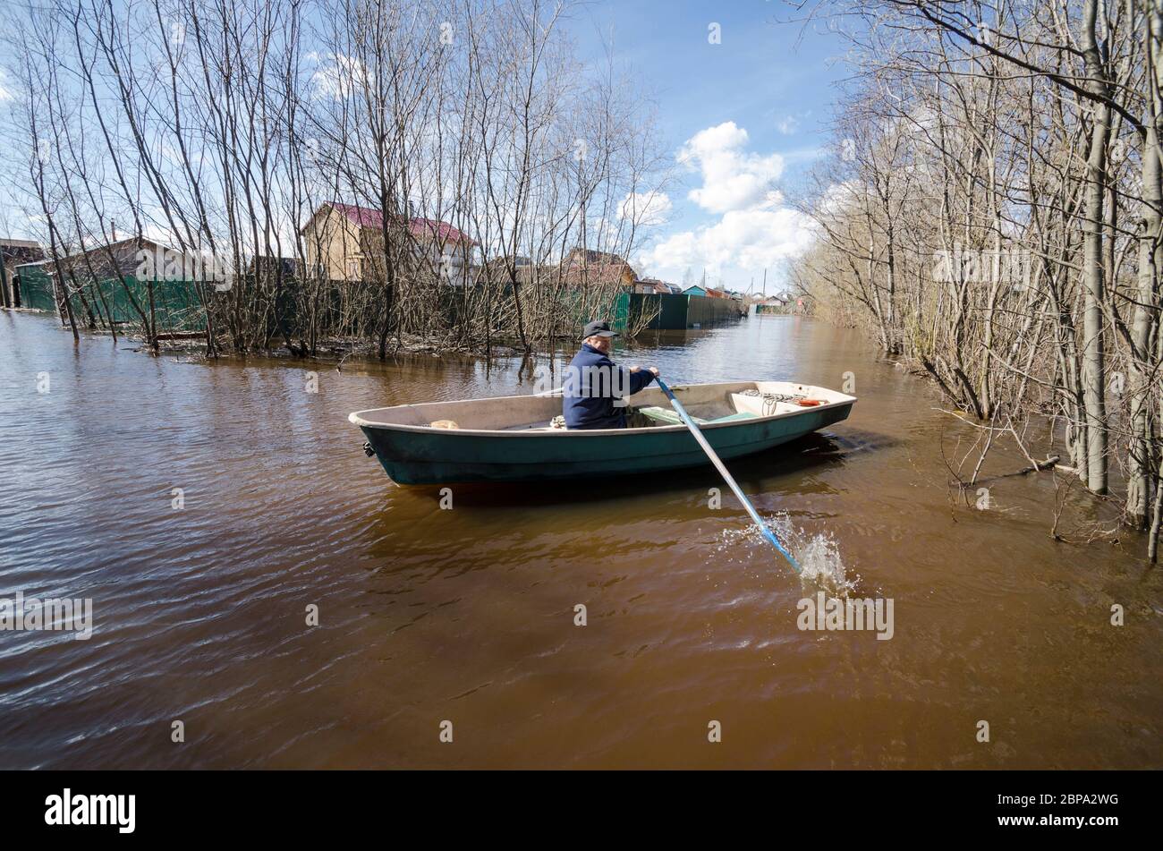 An elderly man rides a boat along a flooded street. Flood Stock Photo ...