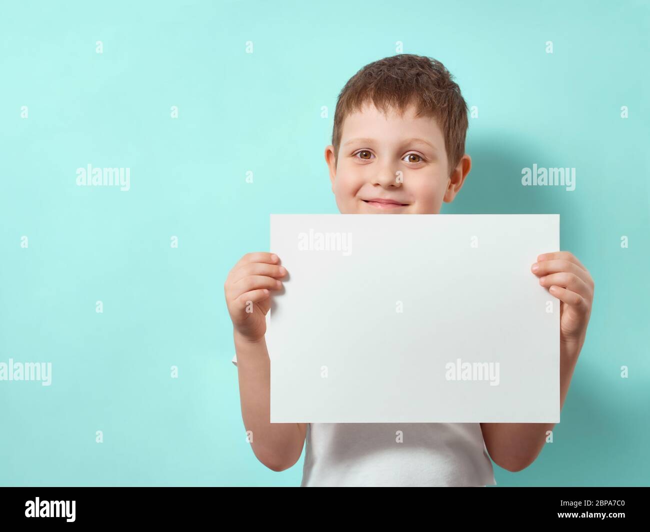 Four-year-old boy smiles and holds blank white paper sheet. Happy child ...