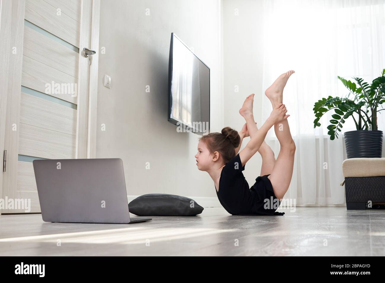 Little girl doing gymnastics exercises at home using online learning ...