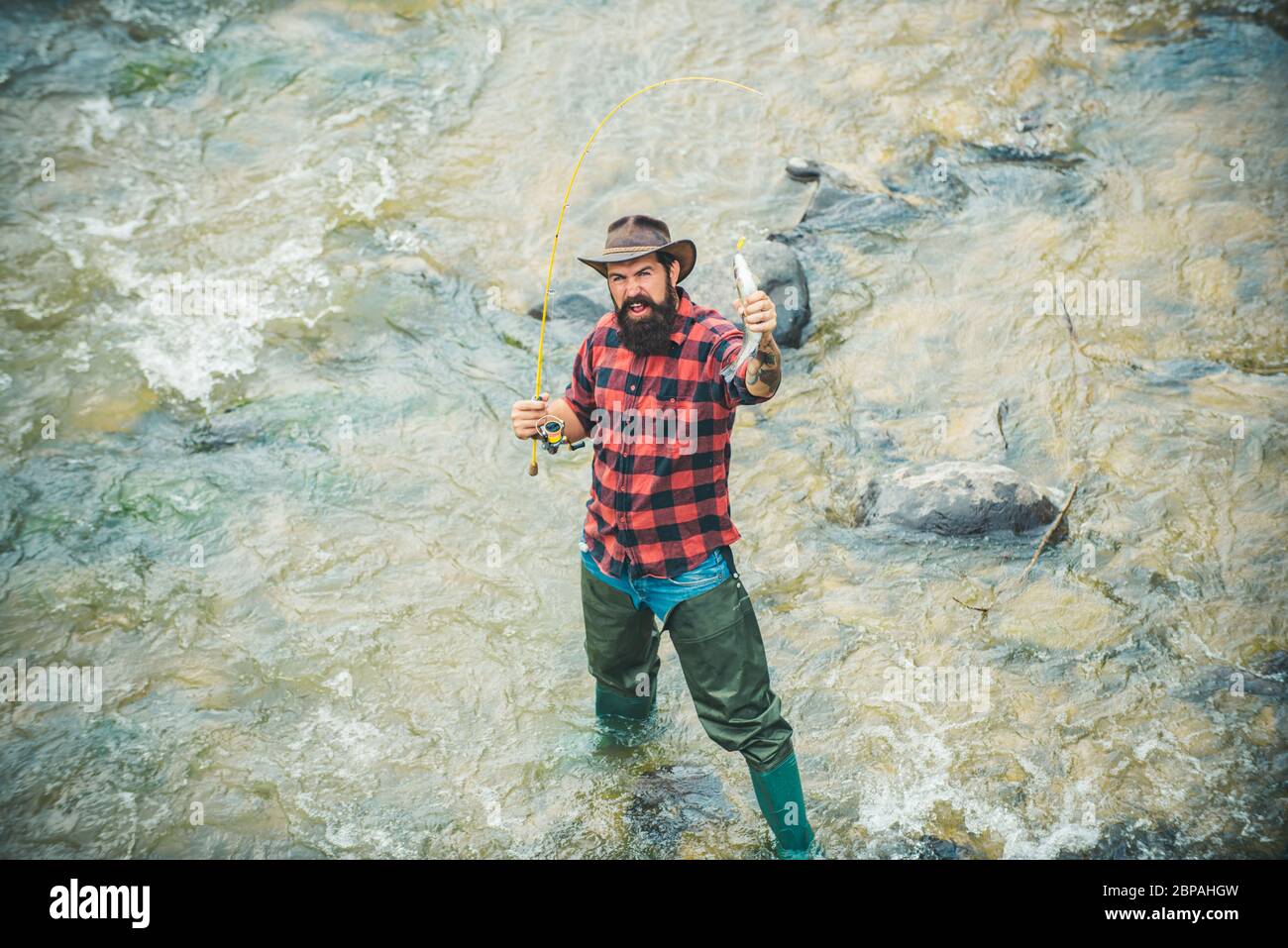 Angler catching the fish. Handsome fisherman in hat and red checkered ...