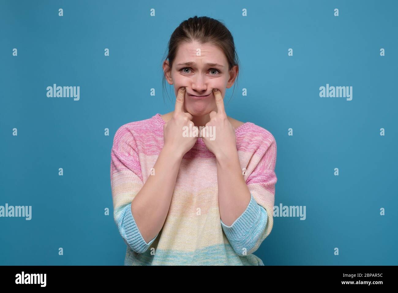 Young upset woman making fake smile with her fingers stretching the ...