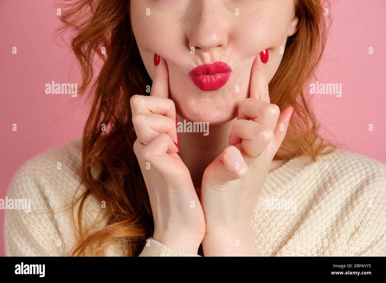 The red-haired girl pulls red lips forward and presses her fingers on ...