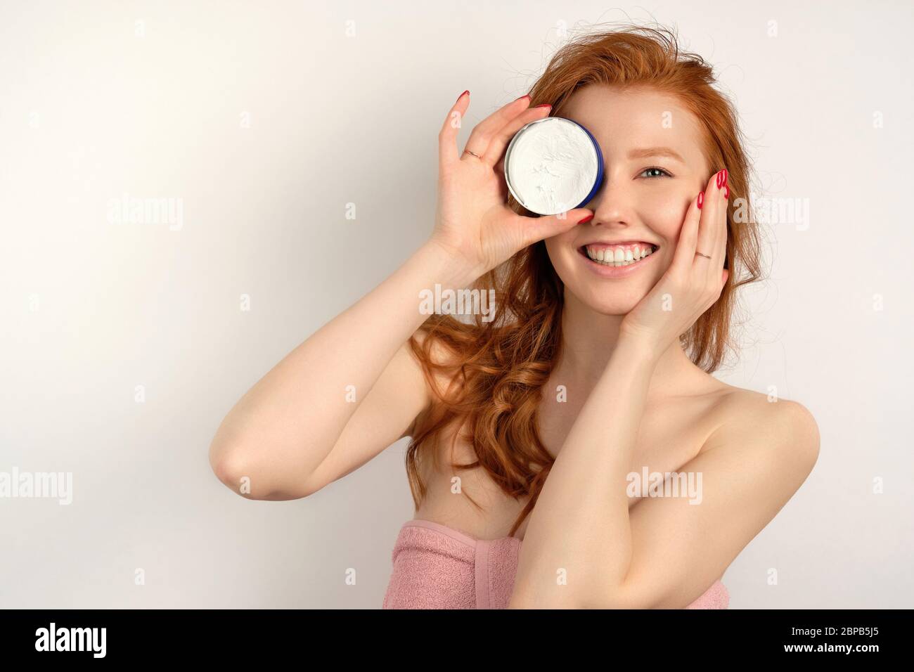 Beautiful red-haired girl with clean skin stands on a white background ...