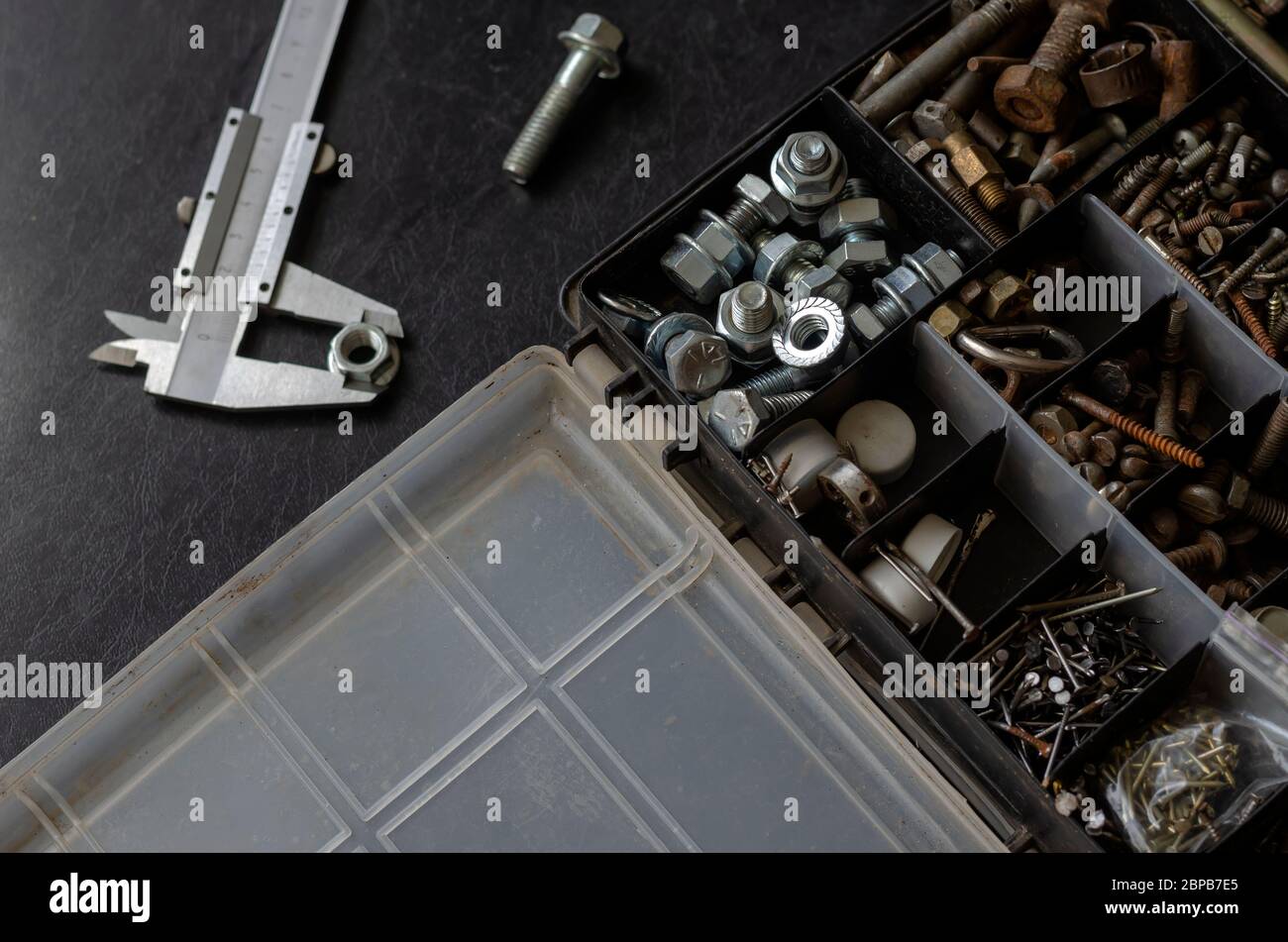 Organizer with bolts and vernier caliper on a black background. Open ...