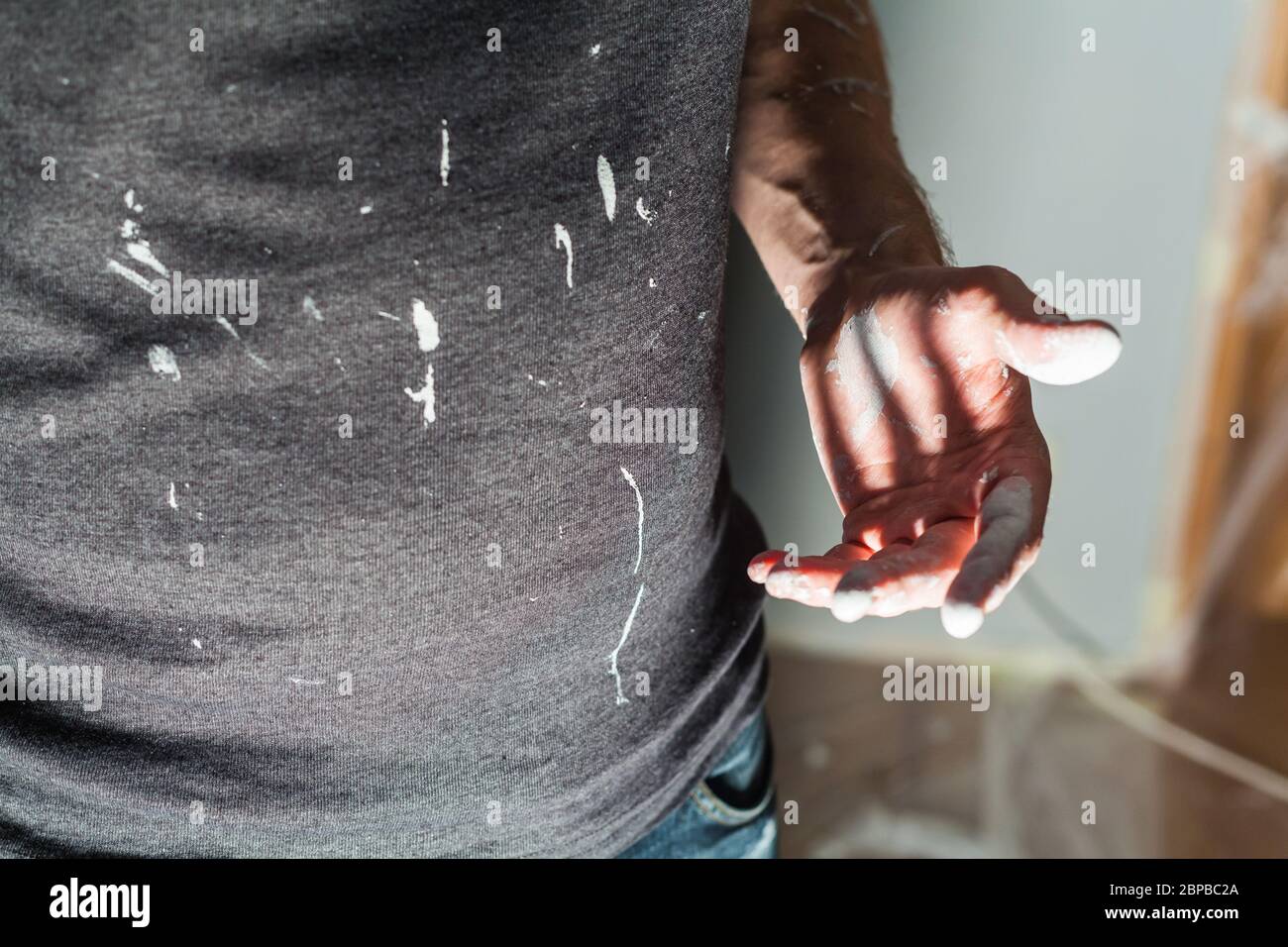 Craftsman with white paint particle at hands and clothes after painting ...
