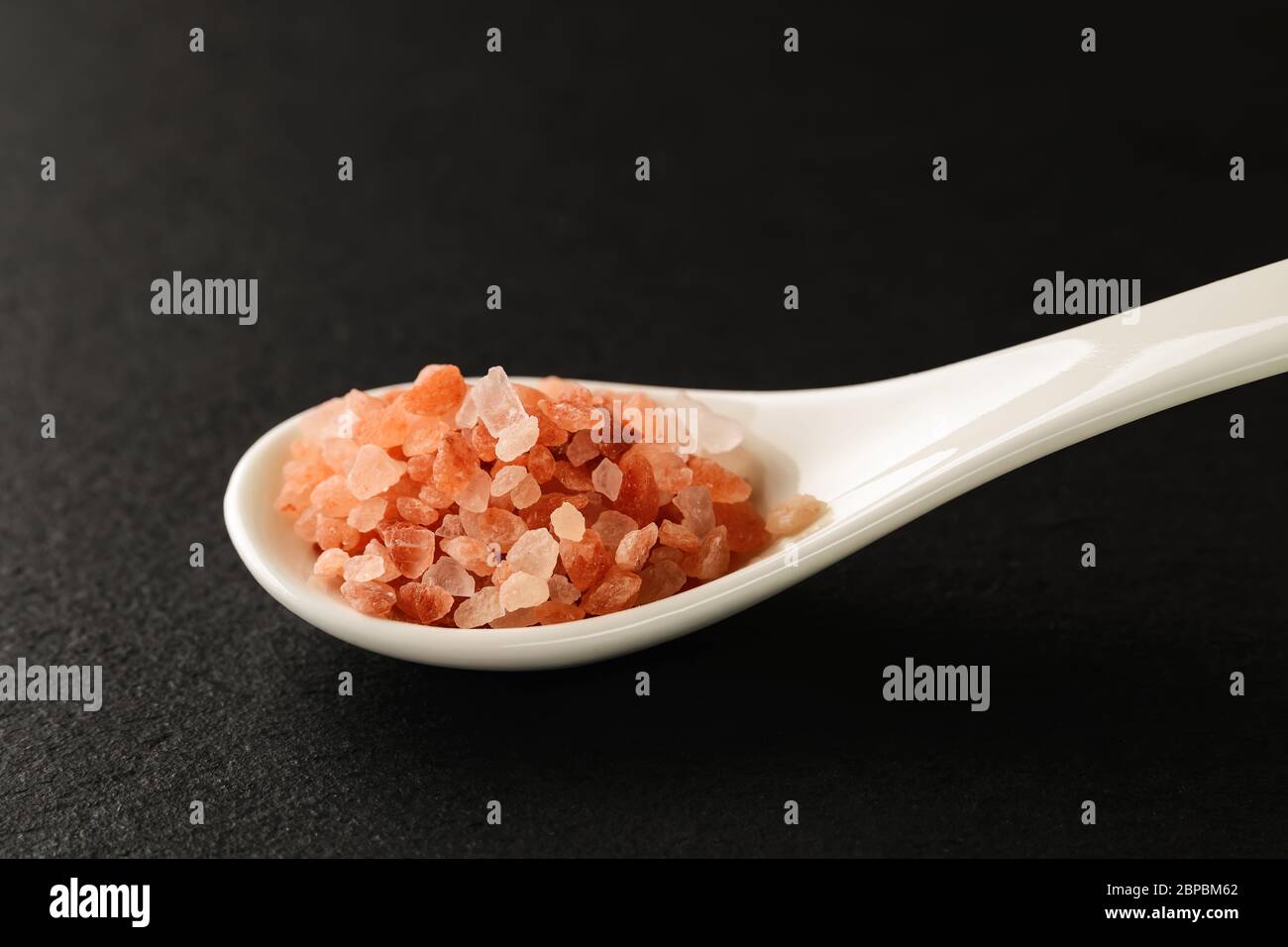 Pink himalayan salt in a white chinese porcelain spoon on a black stone ...