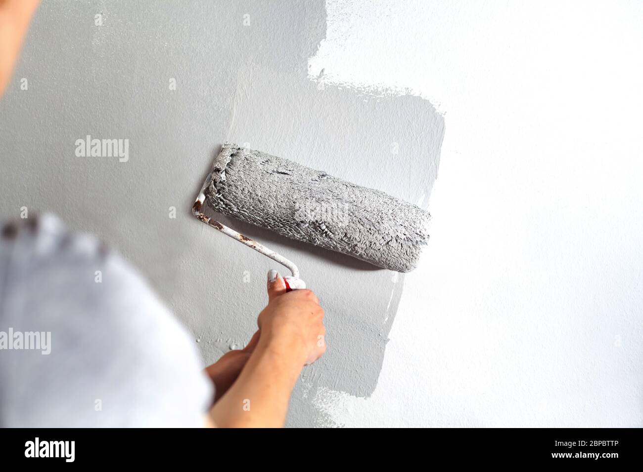 Human hand with large roller of paint begins to paint a white wall ...