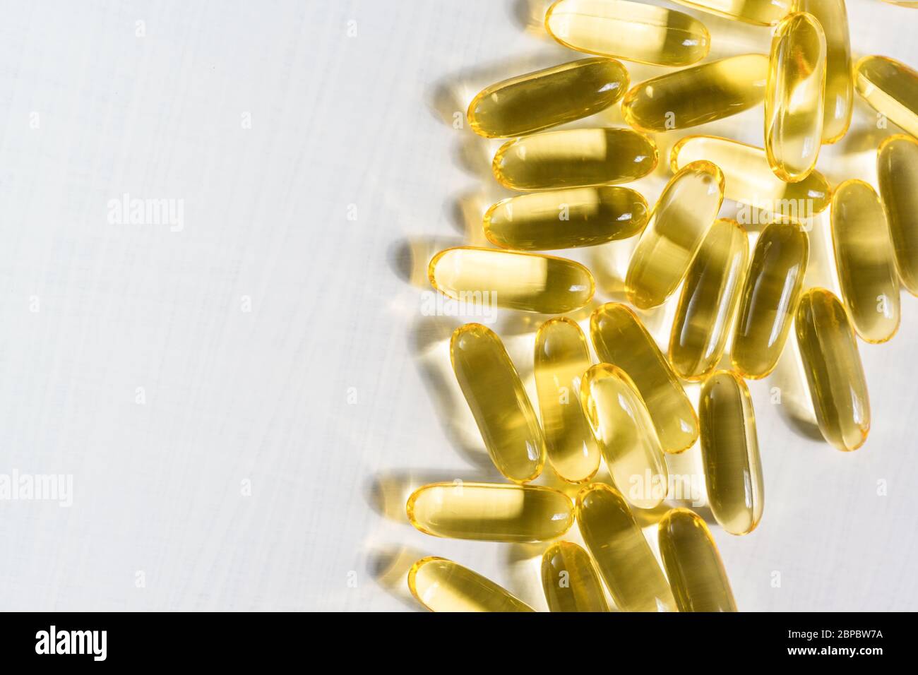 Transparent gelatin capsules with fish oil are on a white table. Omega ...